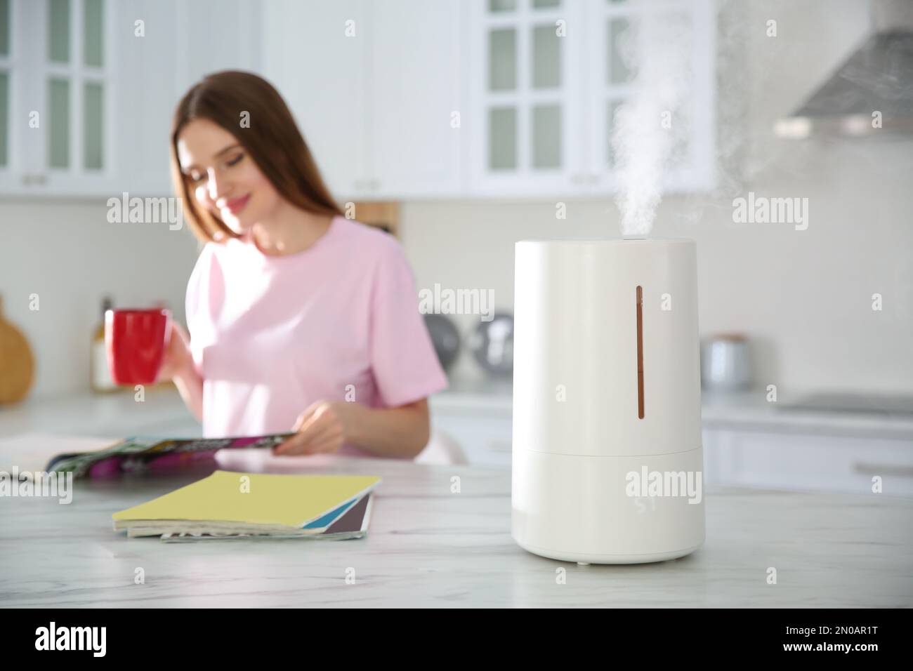 Modern air humidifier and blurred woman drinking coffee in kitchen ...