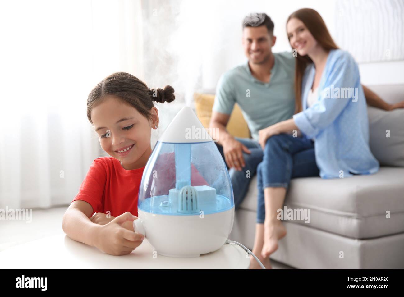 Little girl using modern air humidifier near her parents at home Stock ...