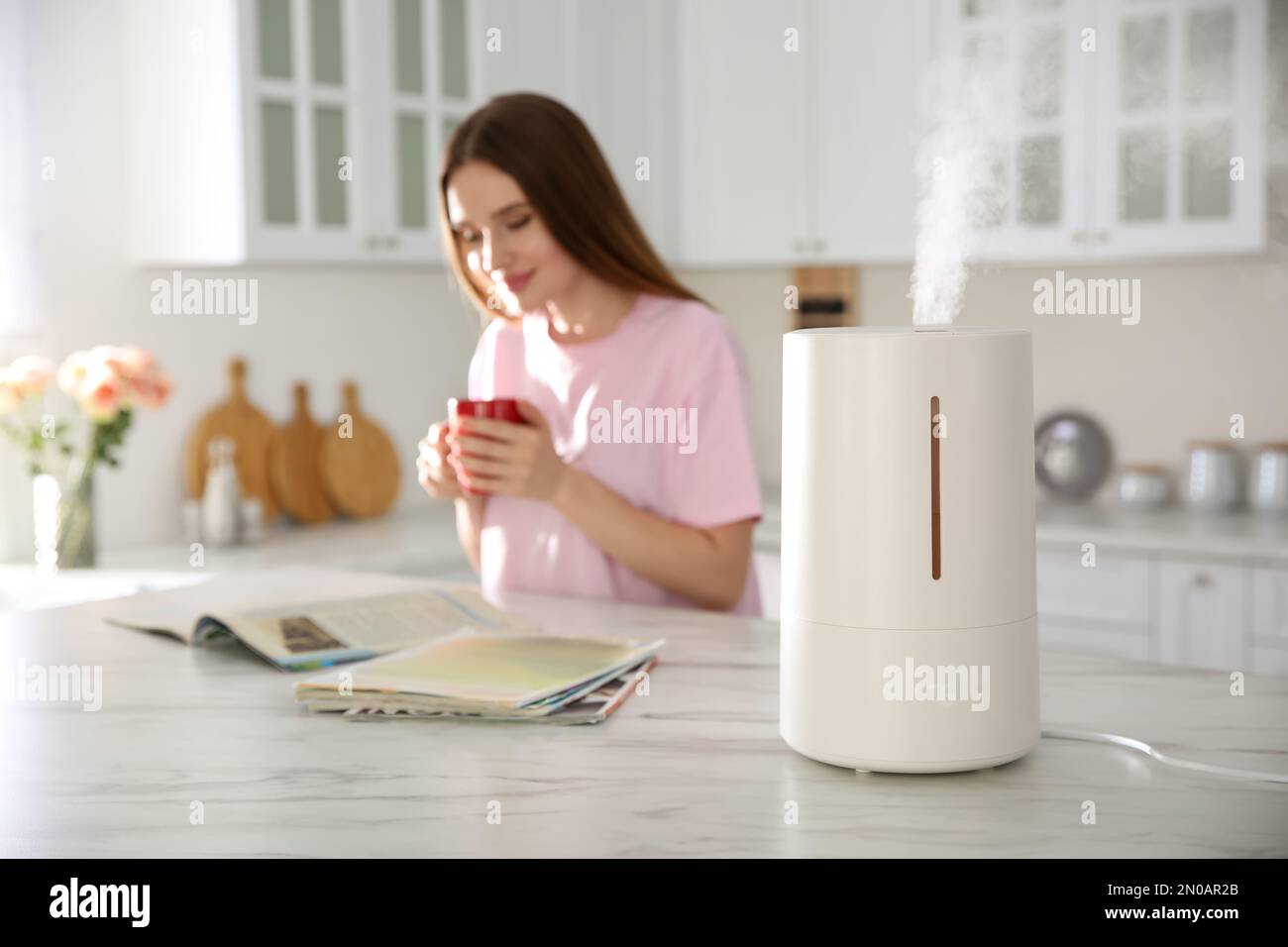 Modern air humidifier and blurred woman drinking coffee in kitchen ...