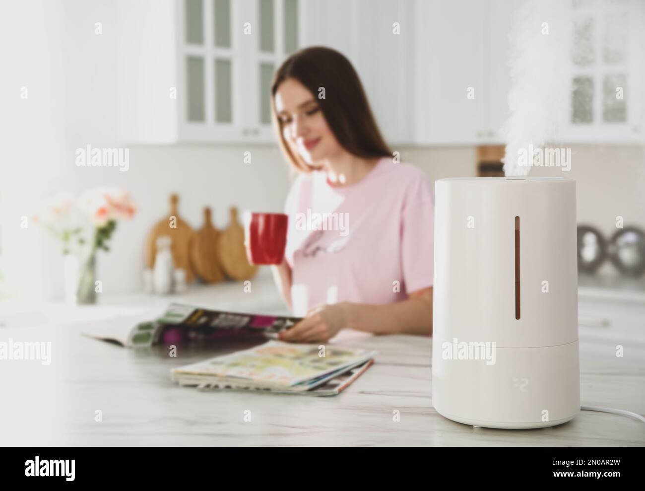 Modern air humidifier and blurred woman drinking coffee in kitchen ...