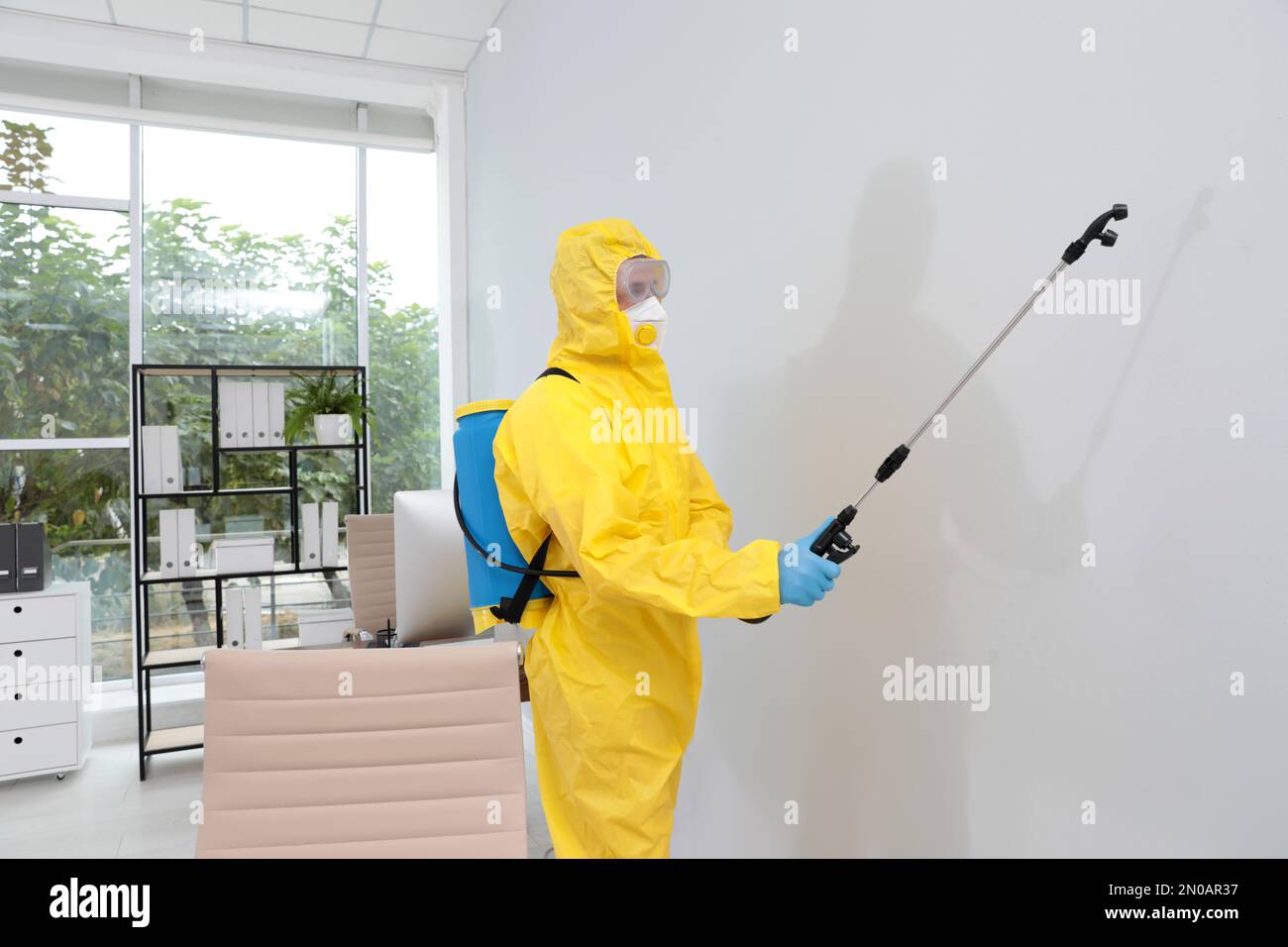 Janitor in protective suit disinfecting office to prevent spreading of ...