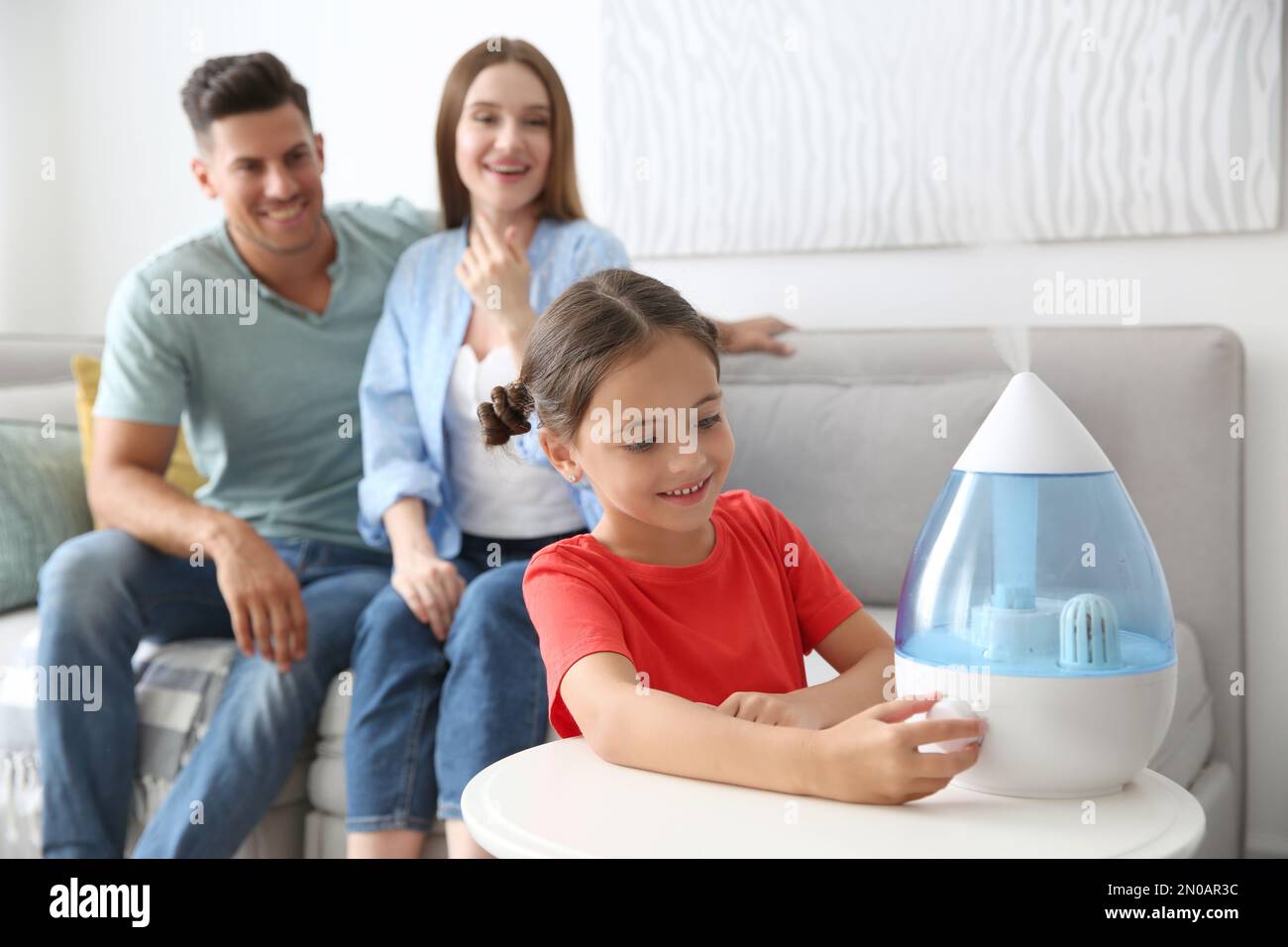 Little girl using modern air humidifier near her parents at home Stock ...