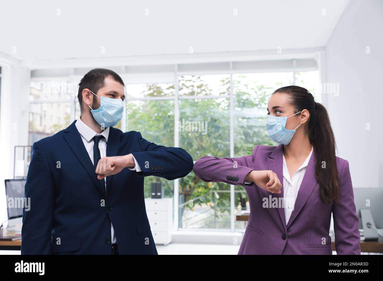 Office employees in masks greeting each other by bumping elbows at ...