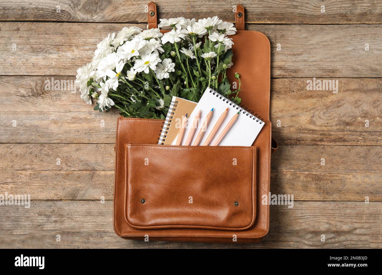 Leather briefcase with stationery and flowers on wooden table, top view ...