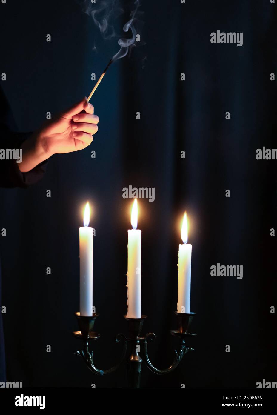 Hand igniting candles with match stick on the dark background ...