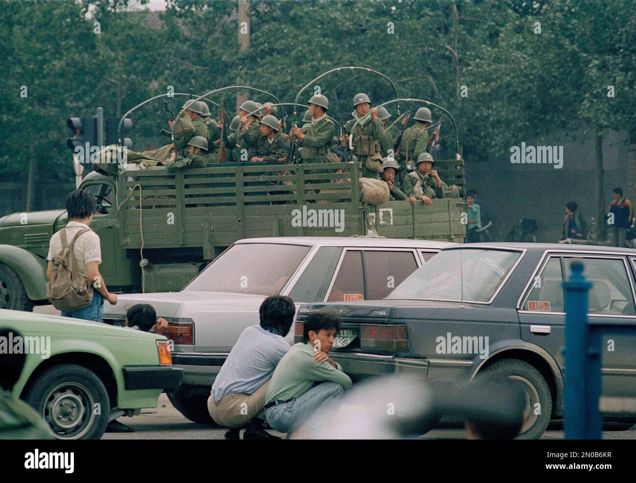 Two people hide behind a car as a truckload of PLA soldiers pass by ...