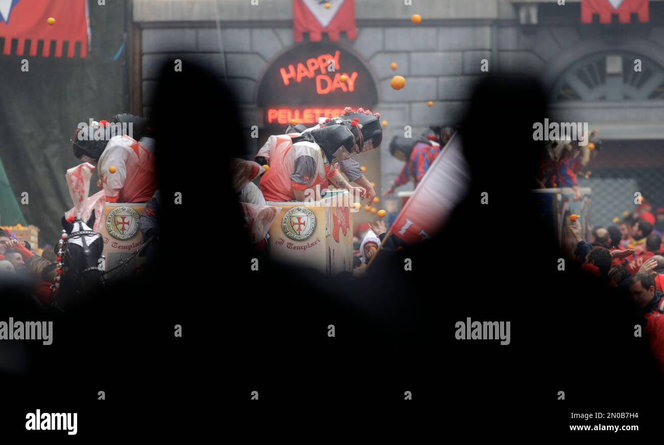Costumed revelers in protective helmets throw oranges during Carnival ...