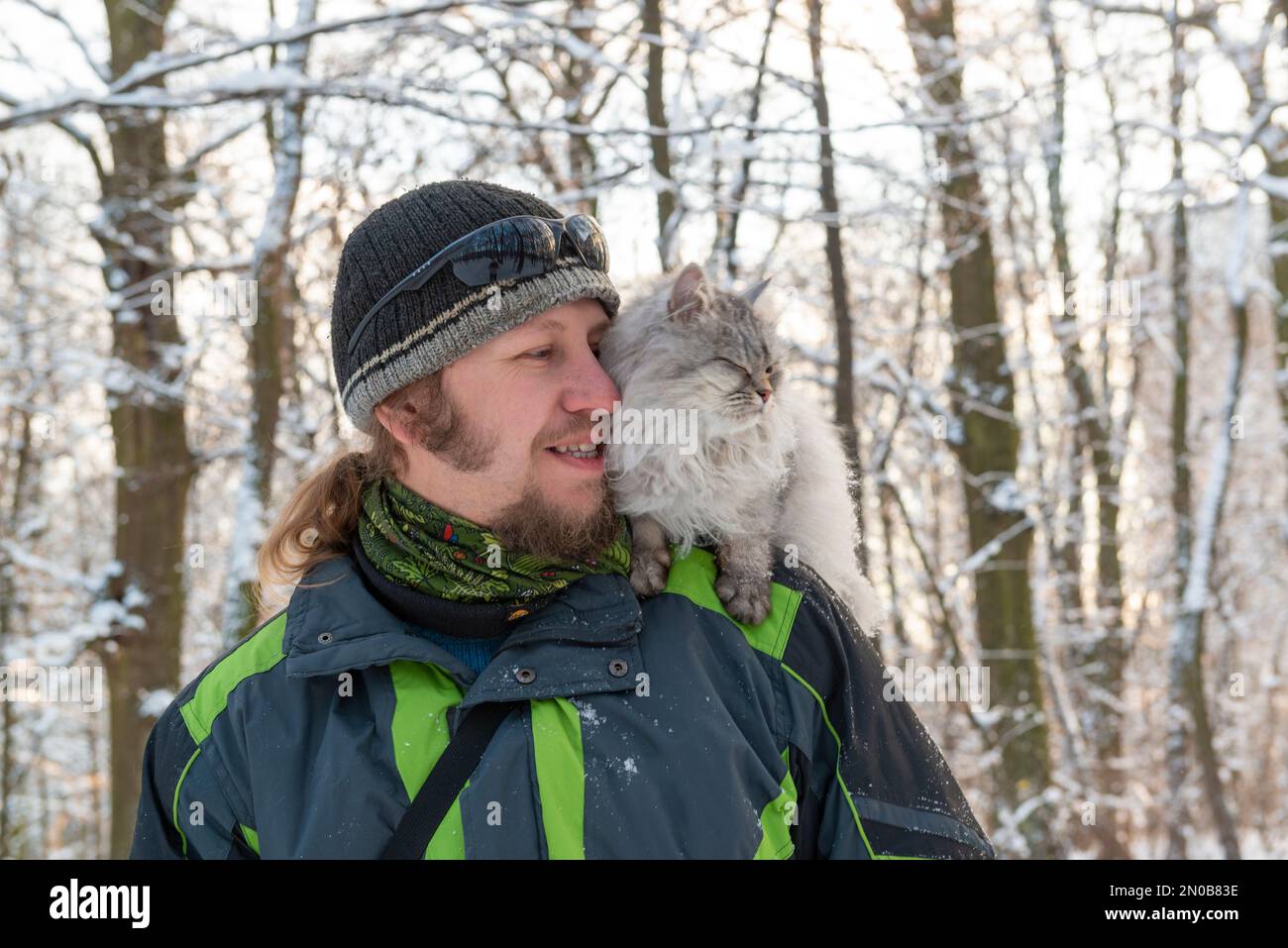 Bearded man with cute cat on the shoulder on a walk in the sunny park ...