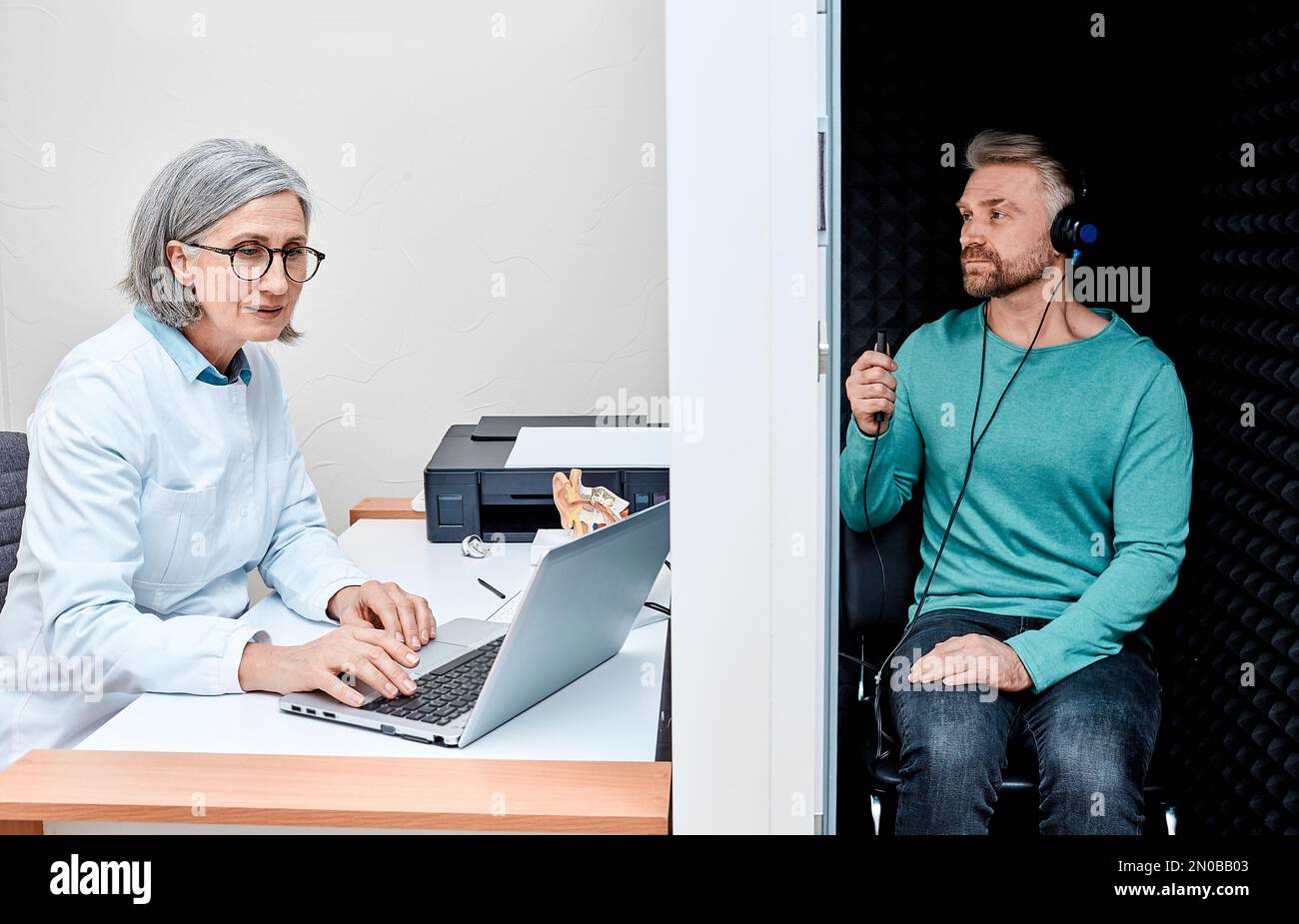 Male patient sitting in audiology booth receives hearing exam and ...