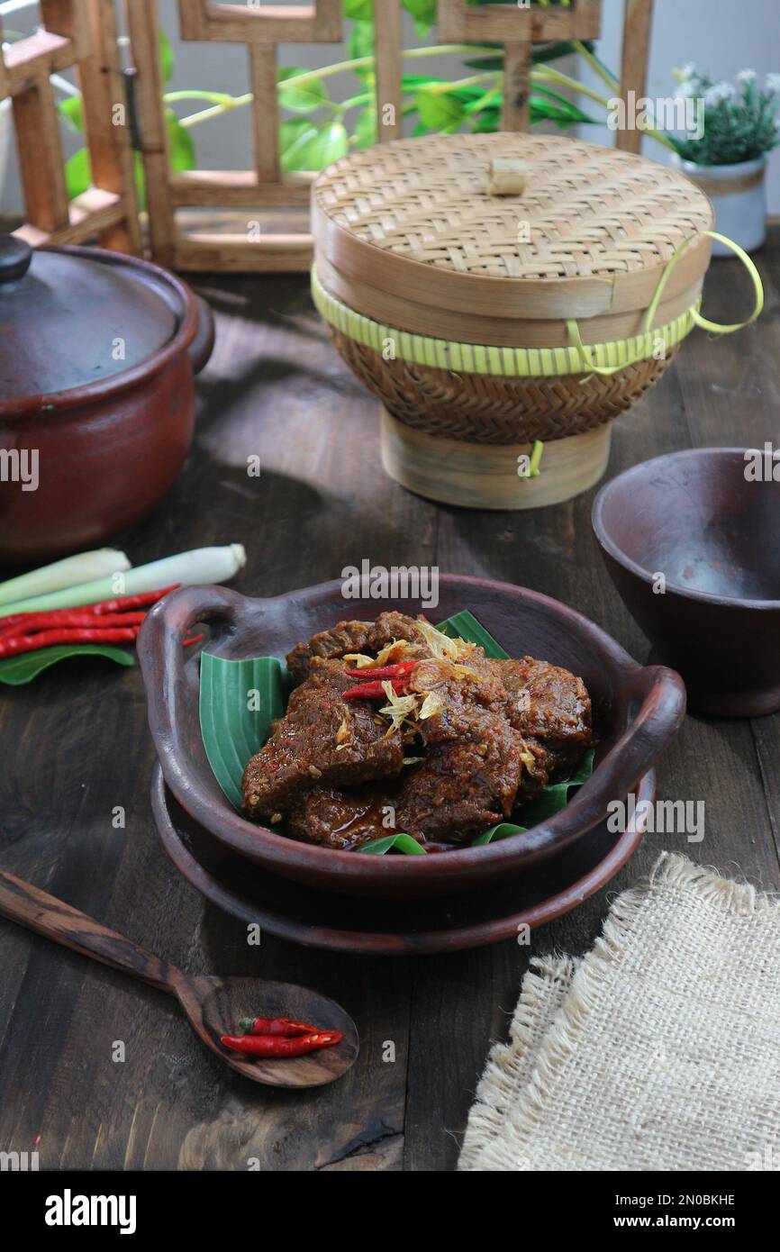 beef rendang in a clay bowl against a background of woven bamboo ...