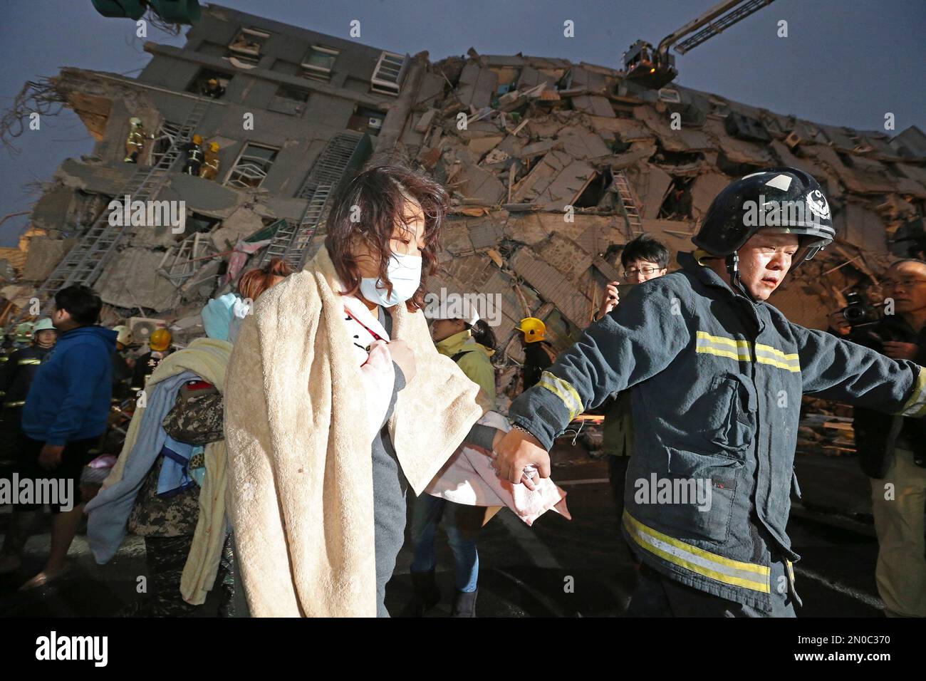 A woman is led by a rescue worker from the site of a toppled building ...