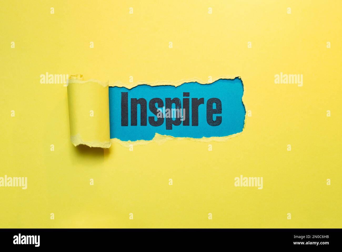 inspire word written with stamp letters, on blue paper seen thru ripped ...
