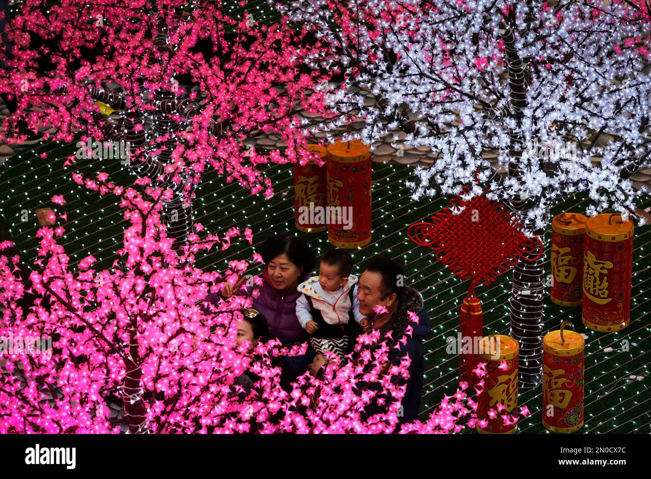 A Chinese family take a selfie in front of trees decorated with light ...
