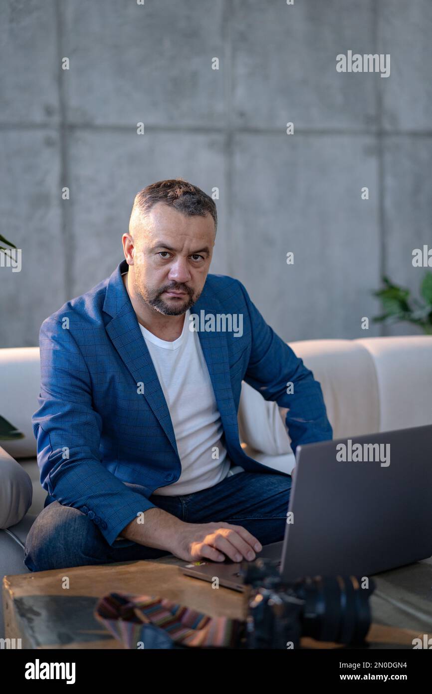 Bearded young confident guy stand behind office desk with laptop thinking working alone ...