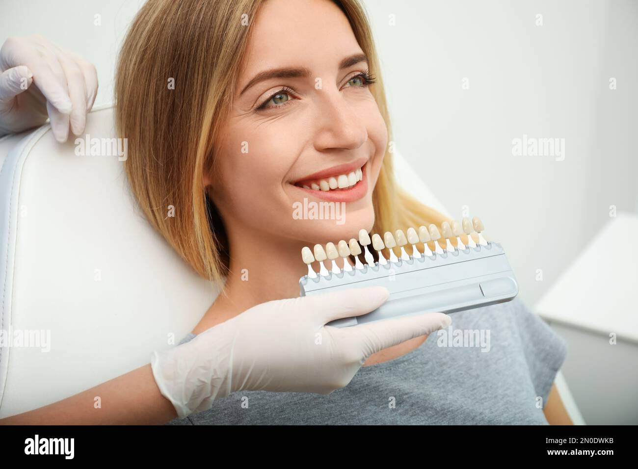 Doctor matching patient's teeth color with palette in clinic, closeup ...