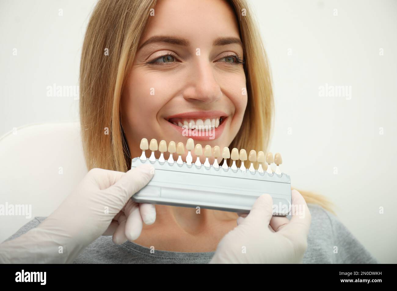 Doctor matching patient's teeth color with palette on light background ...