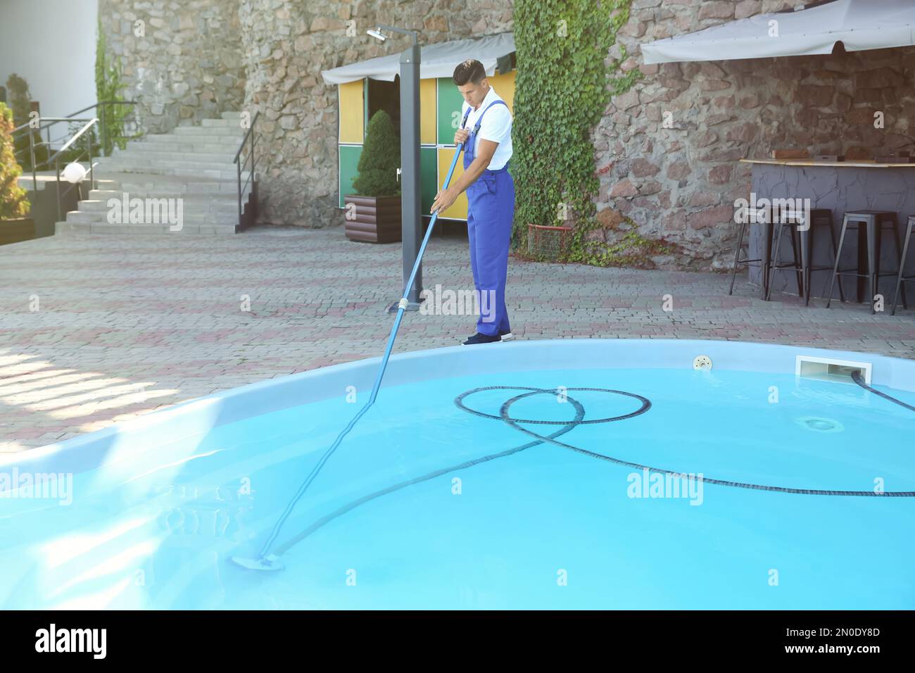 Worker cleaning outdoor swimming pool with underwater vacuum Stock ...