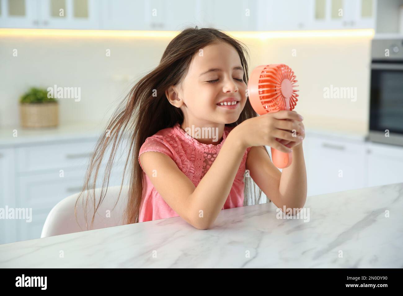 Little girl enjoying air flow from portable fan at home. Summer heat ...