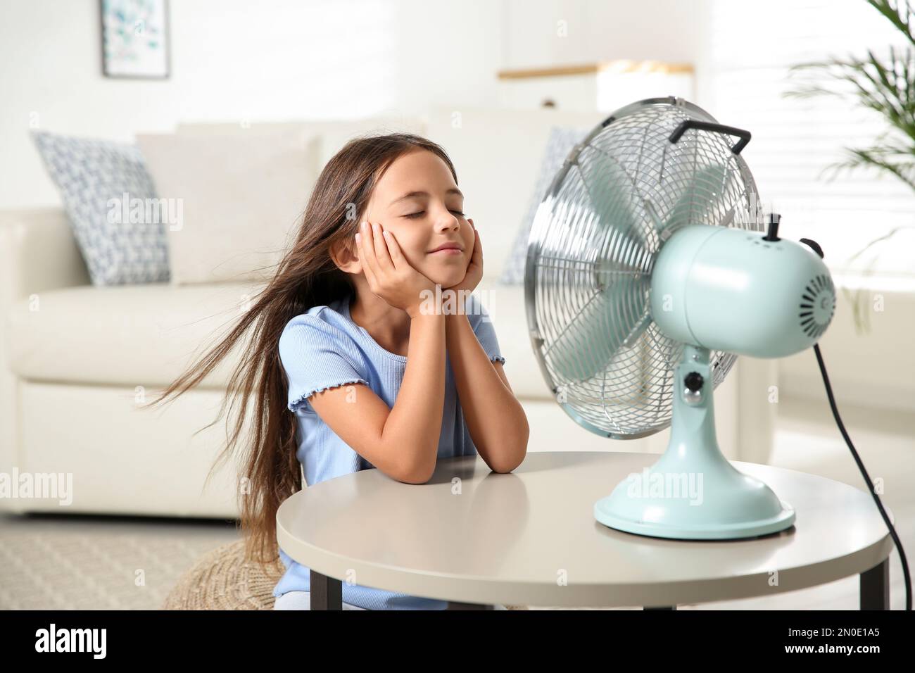 Little girl enjoying air flow from fan at home. Summer heat Stock Photo ...