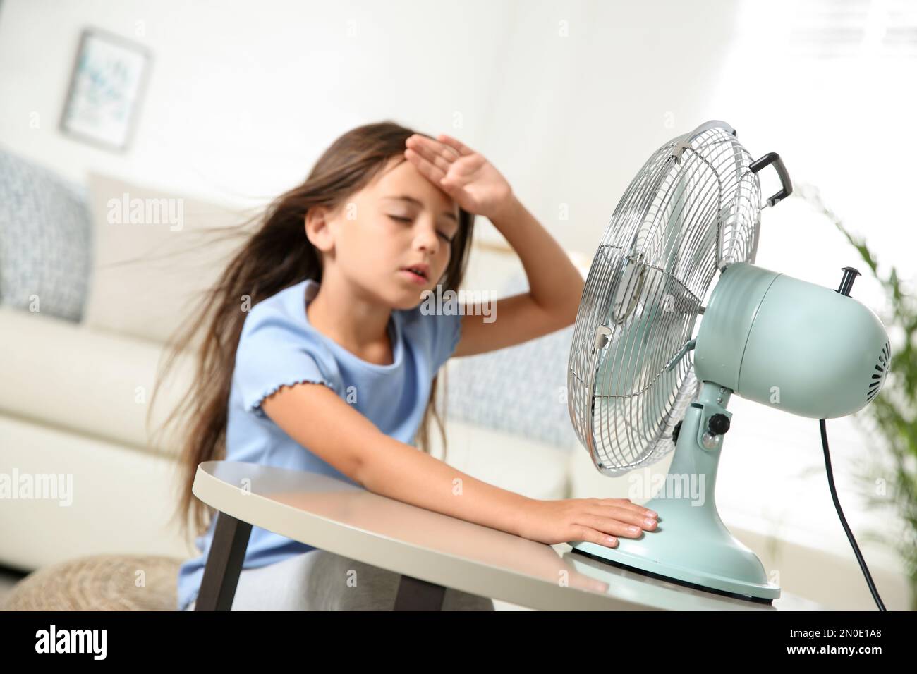 Little girl suffering from heat in front of fan at home. Summer season ...