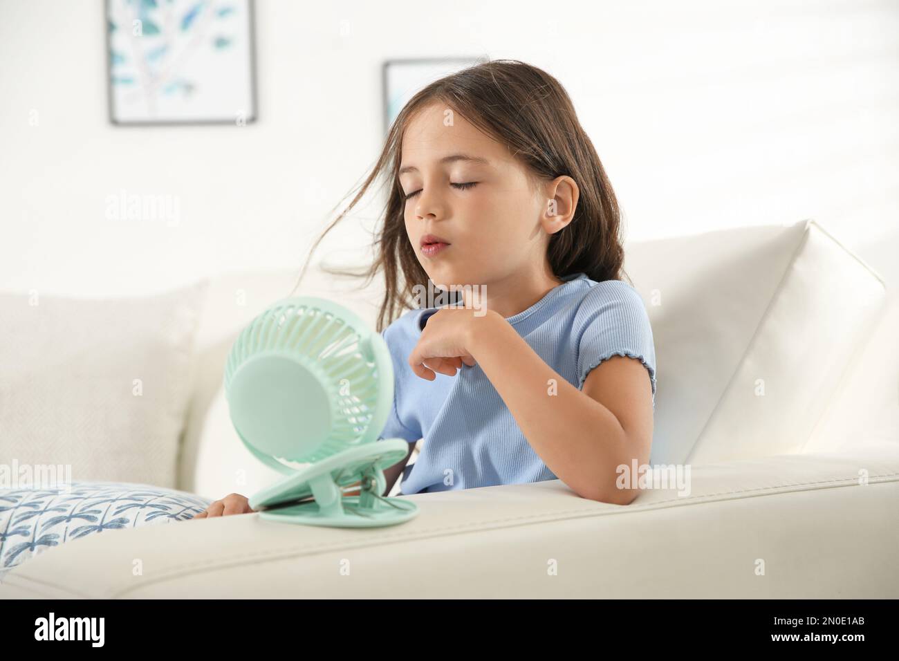 Little girl enjoying air flow from portable fan at home. Summer heat ...