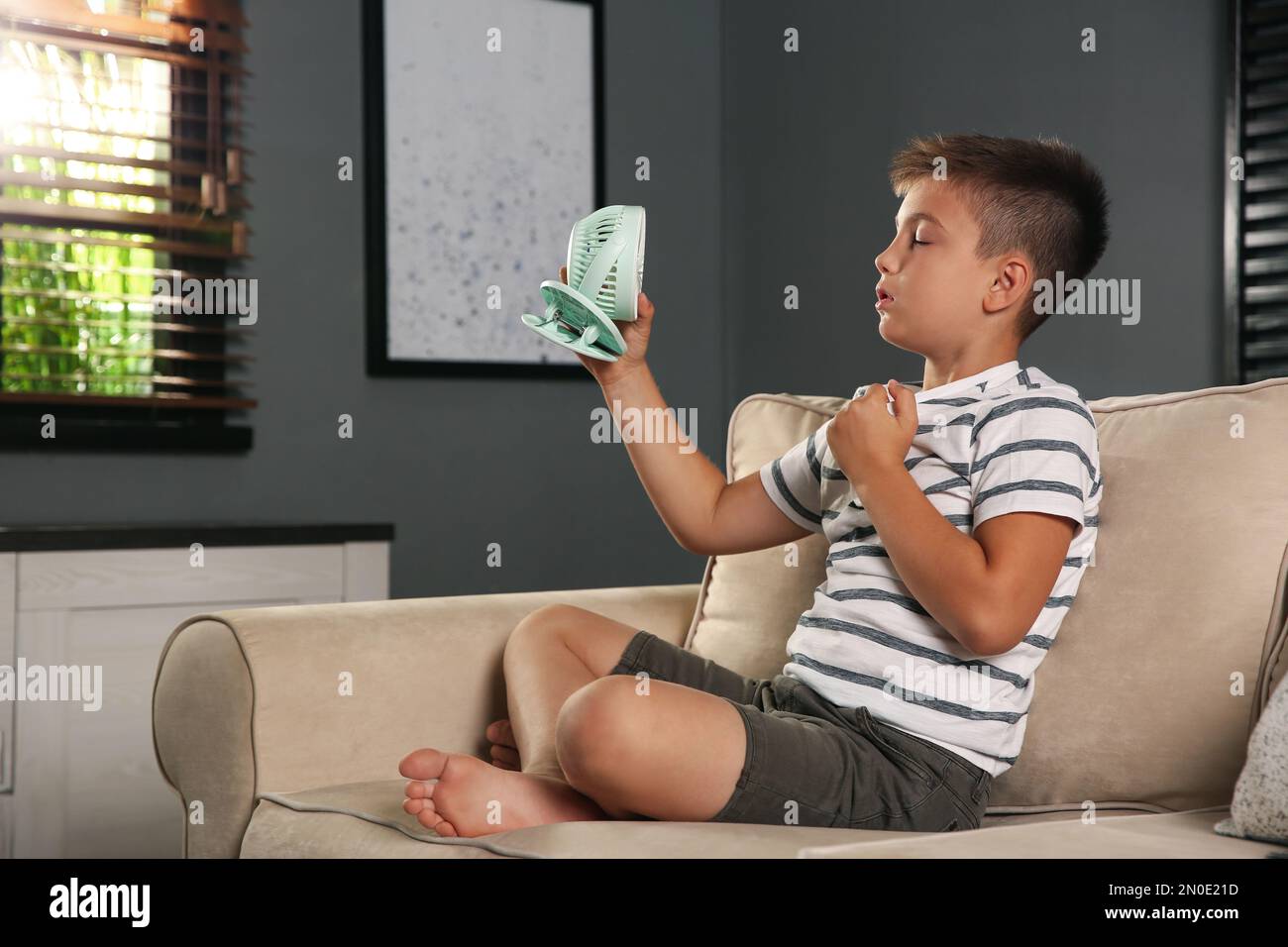 Little boy with portable fan suffering from heat at home. Summer season ...