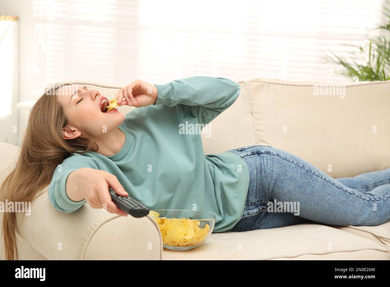 Lazy young woman with bowl of chips watching TV on sofa at home Stock Photo - Alamy