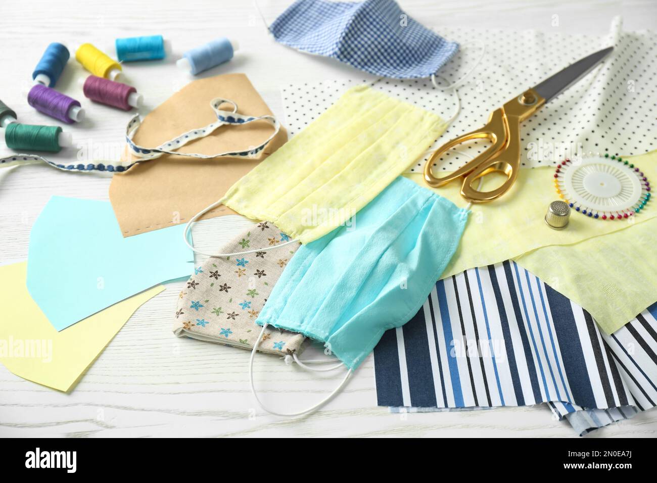 Fabric, sewing accessories and cloth masks on white wooden table ...