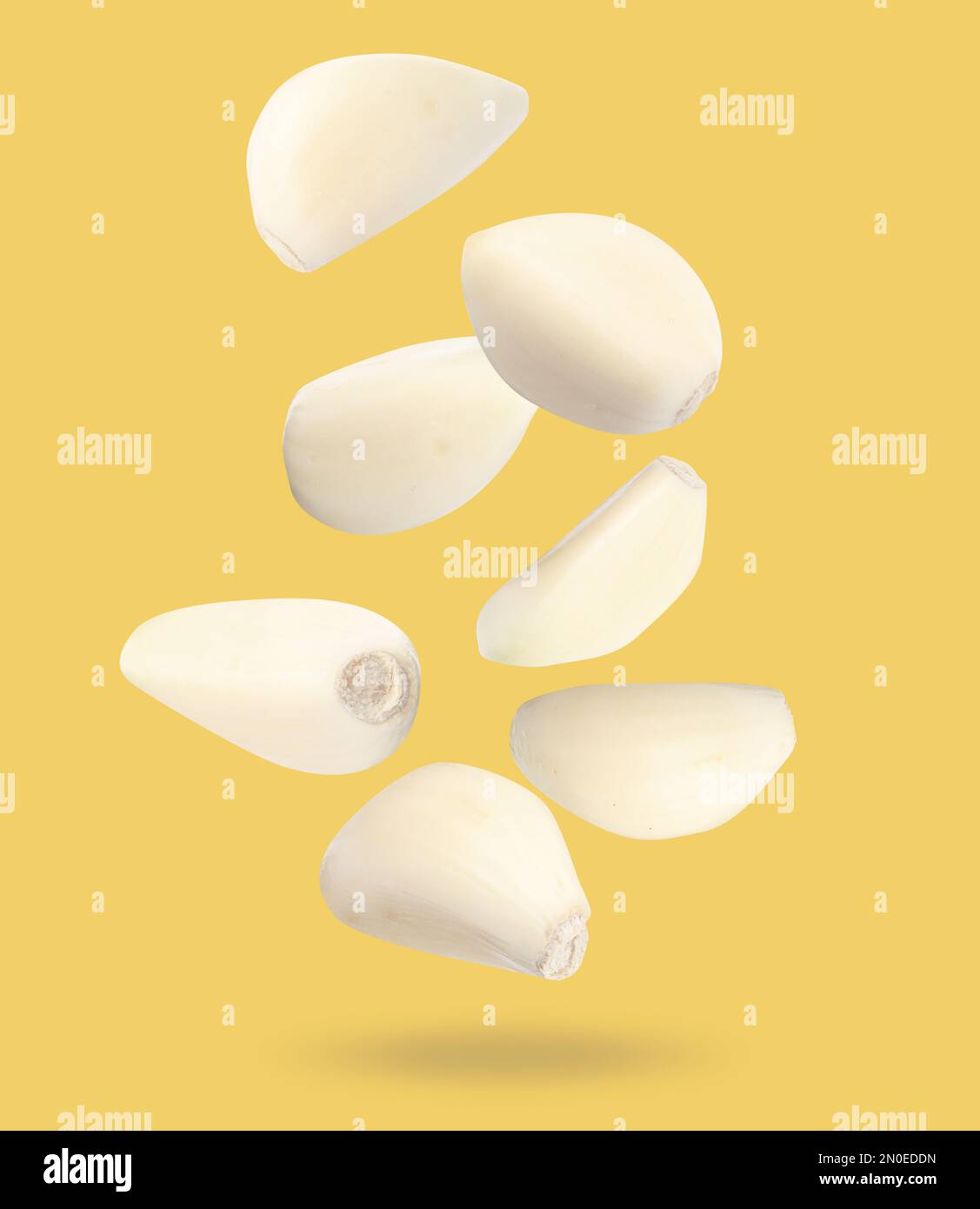 Many garlic cloves falling on yellow background Stock Photo - Alamy