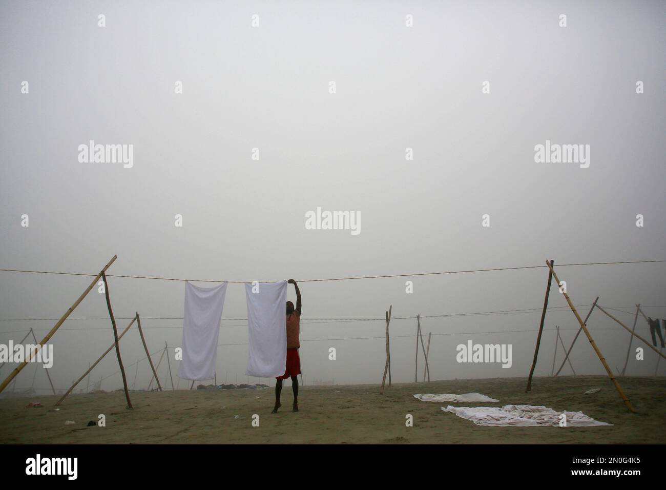 An Indian washerman hangs clothes for drying on the banks of the rRiver ...