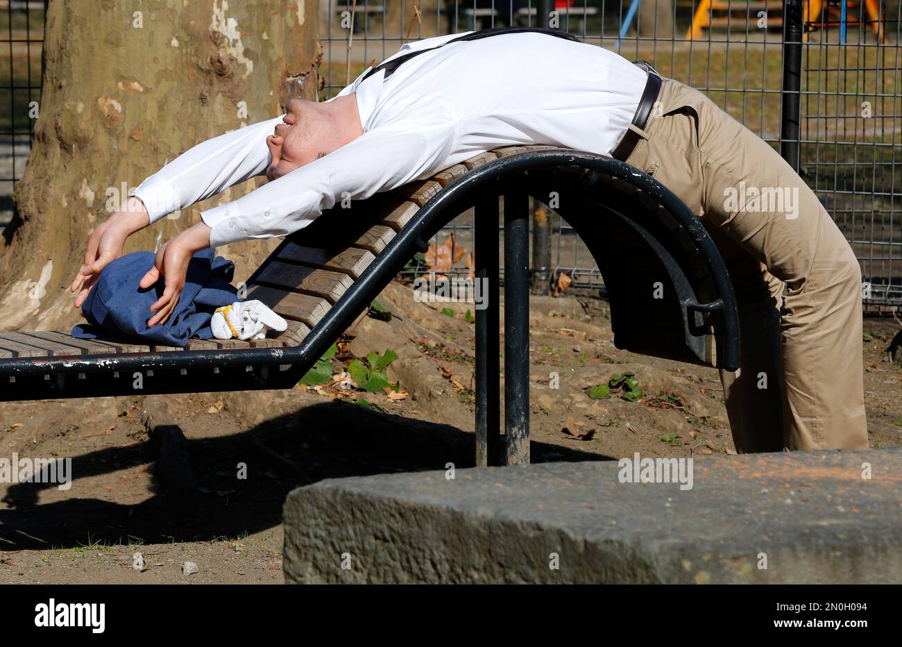 A businessman does a stretch on a sunny bench in Hibiya Park in Tokyo ...