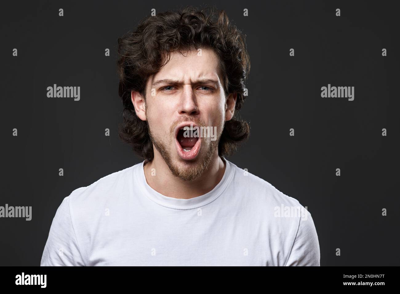 annoyed angry curly bearded man on dark gray studio background Stock ...