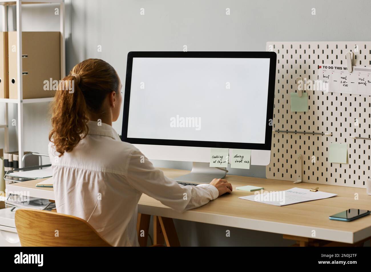 Back view of young woman using computer with white screen mockup while ...