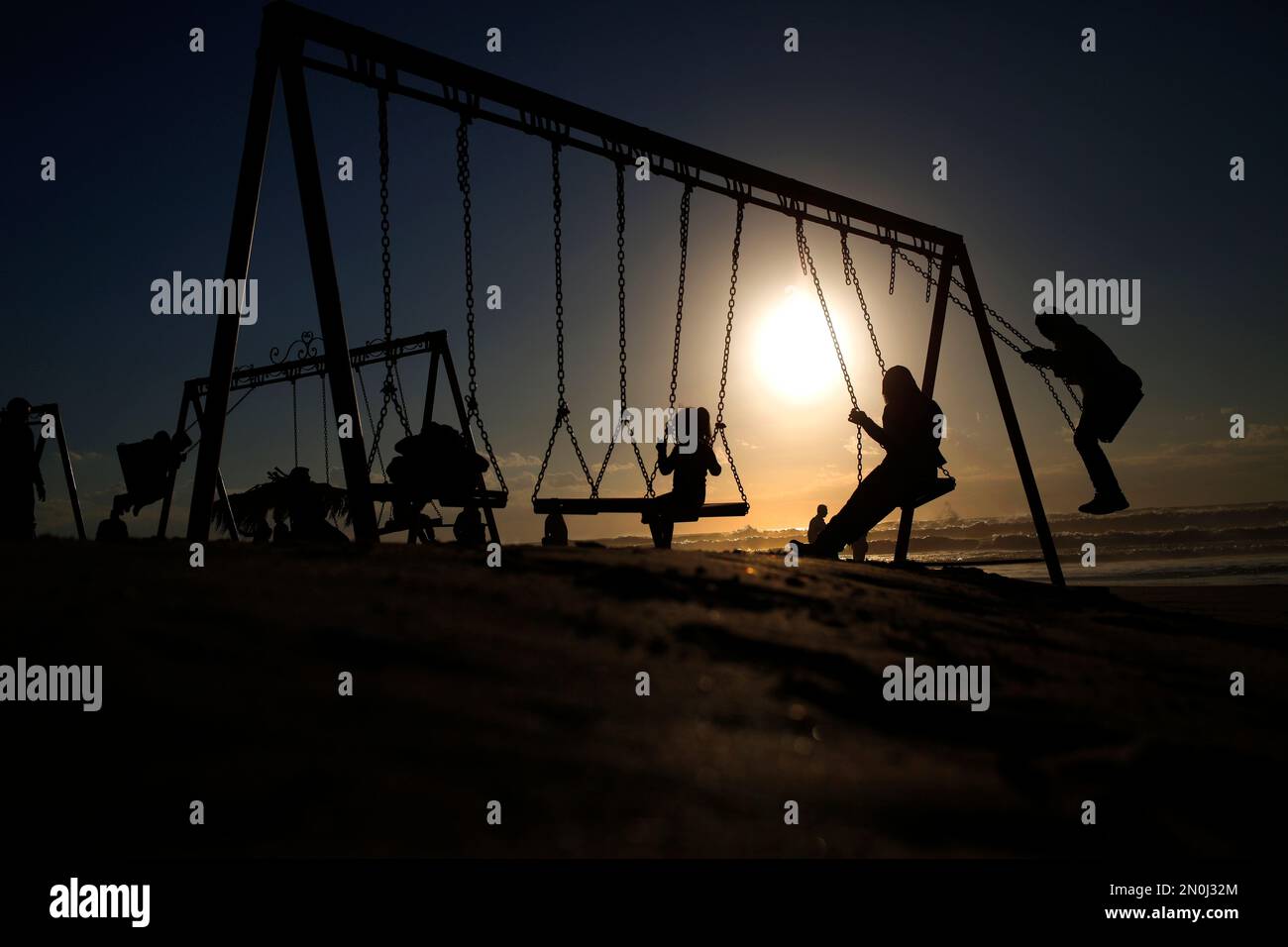 A Syrian refugee family plays on a swing as the sun sets, at the Ramlet ...