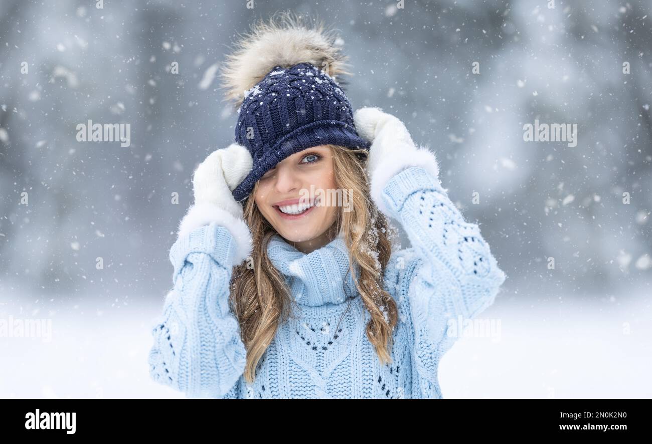 A cute young woman is enjoying the winter and snow, putting on a hat in ...