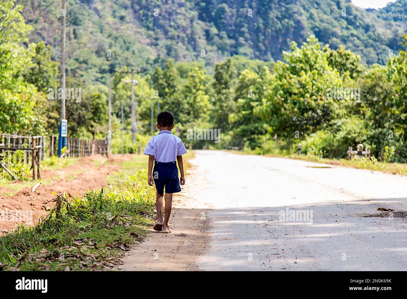 Asian boy walking on the side of the road with the mountains and many ...