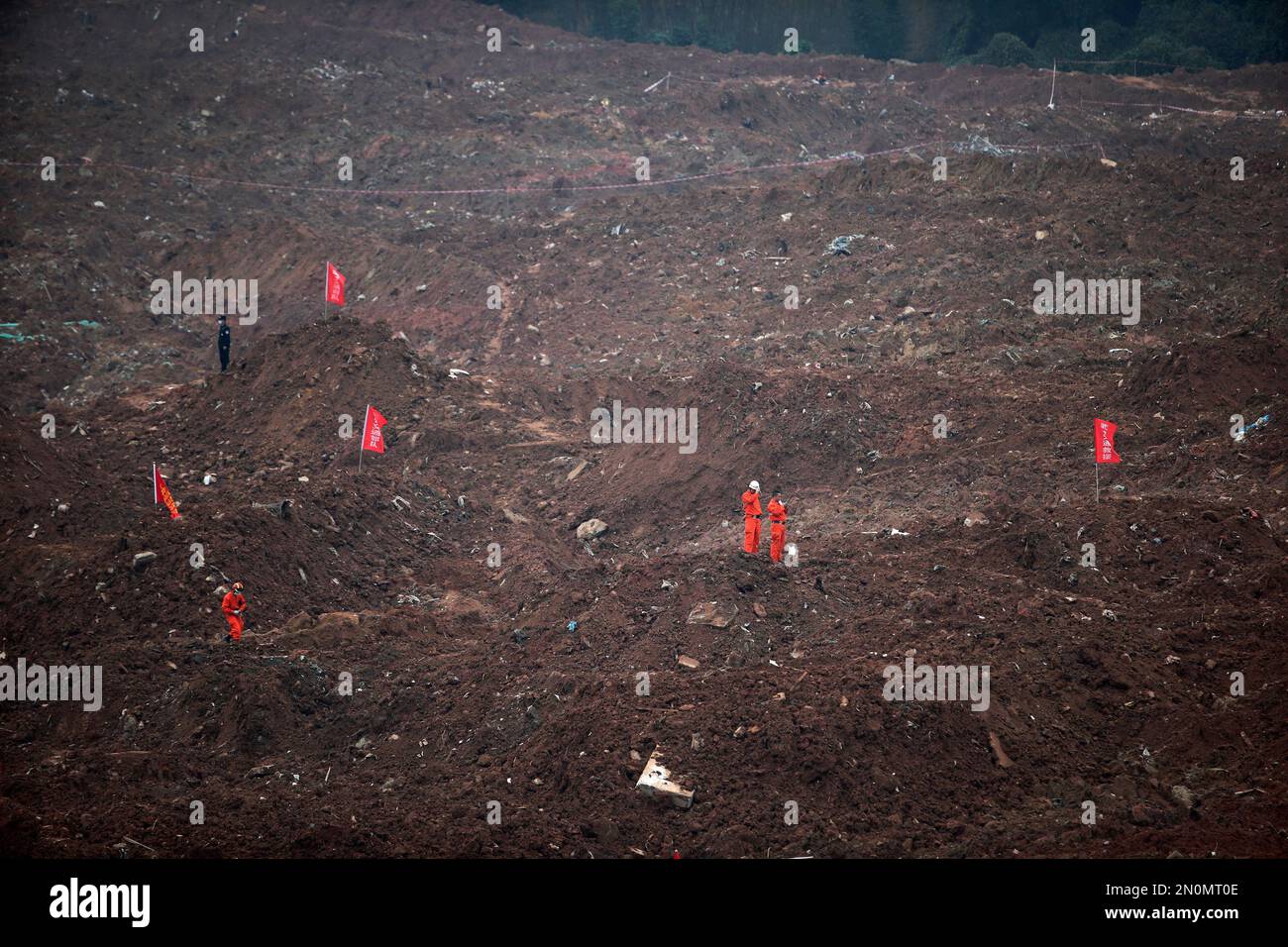 Rescuers stand on the sea of red mud as they search for survivors ...