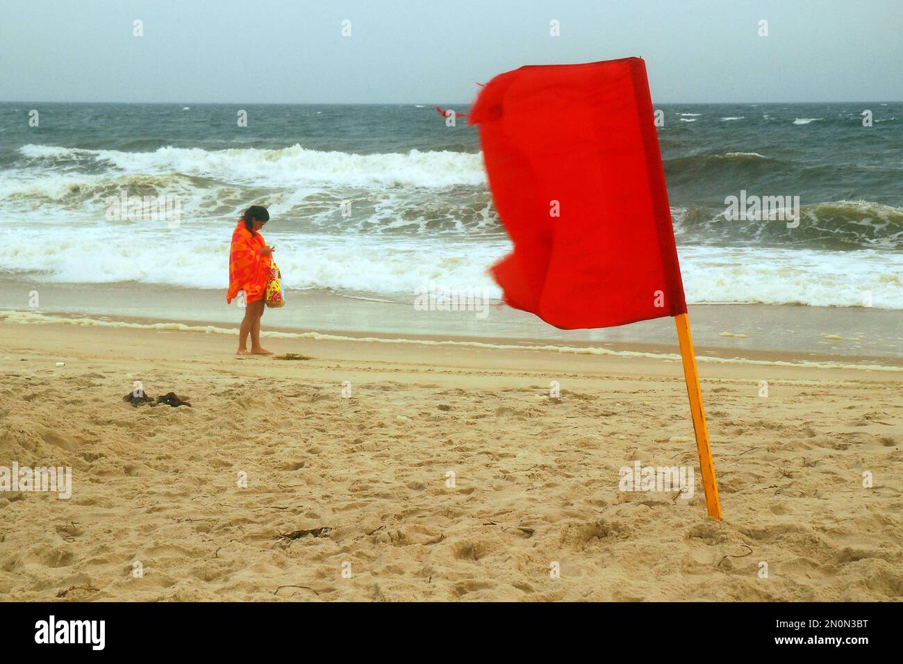 A young woman walks near the shoreline during a stormy, windy day at ...