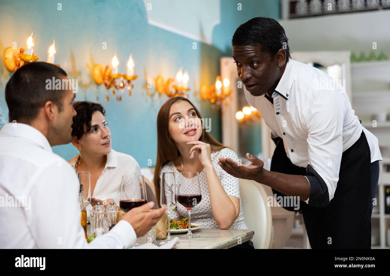 Positive couple talking with polite african american waiter while ...