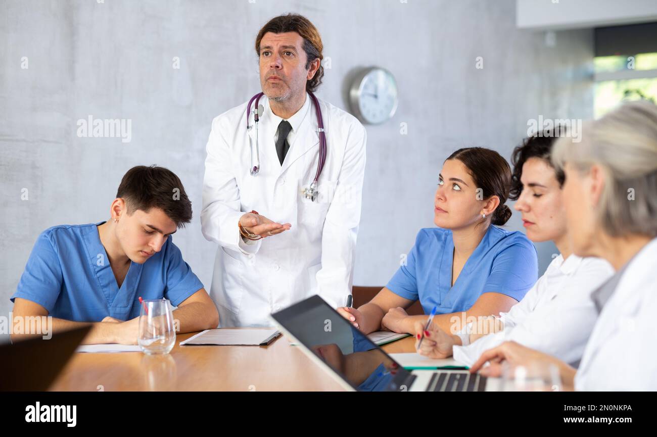 Male chief doctor discussing reports from colleagues of different ages ...