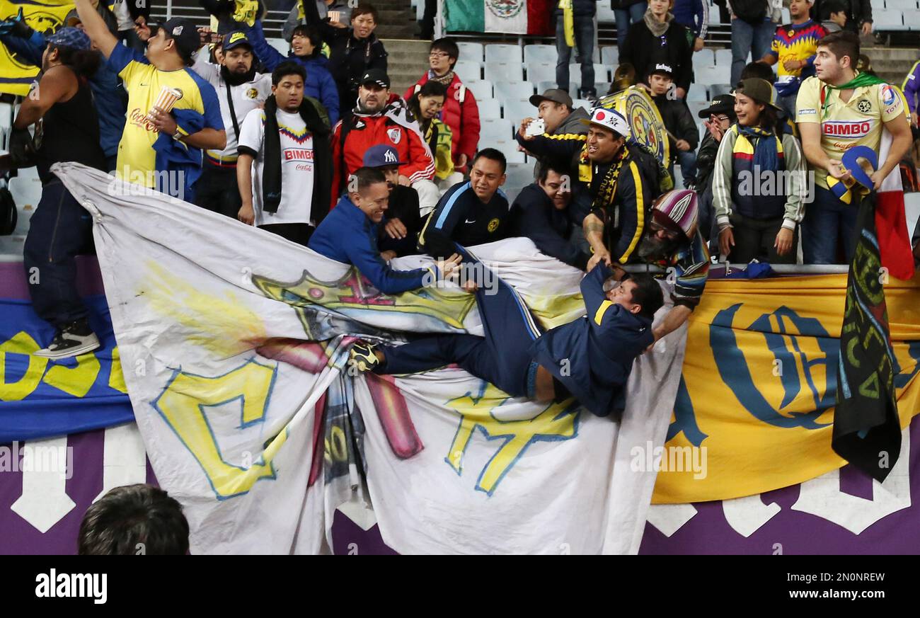 A Club America fan is held by supporters as he falls over a safety rail ...