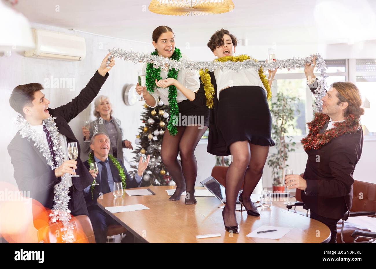 Cheerful young women dancing on table during Christmas party in office ...
