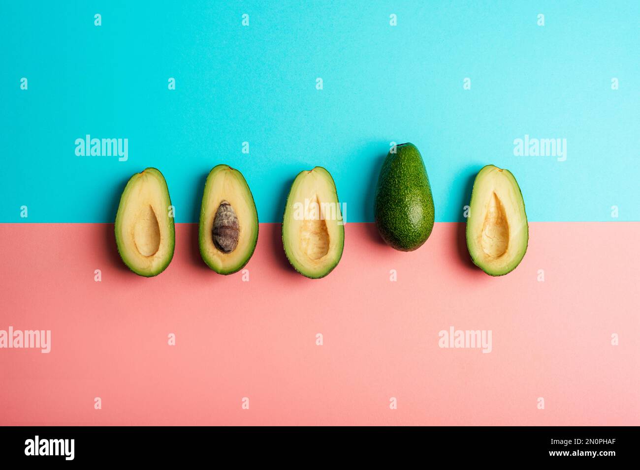 Avocado halves and whole avocado fruit on pink and blue background ...