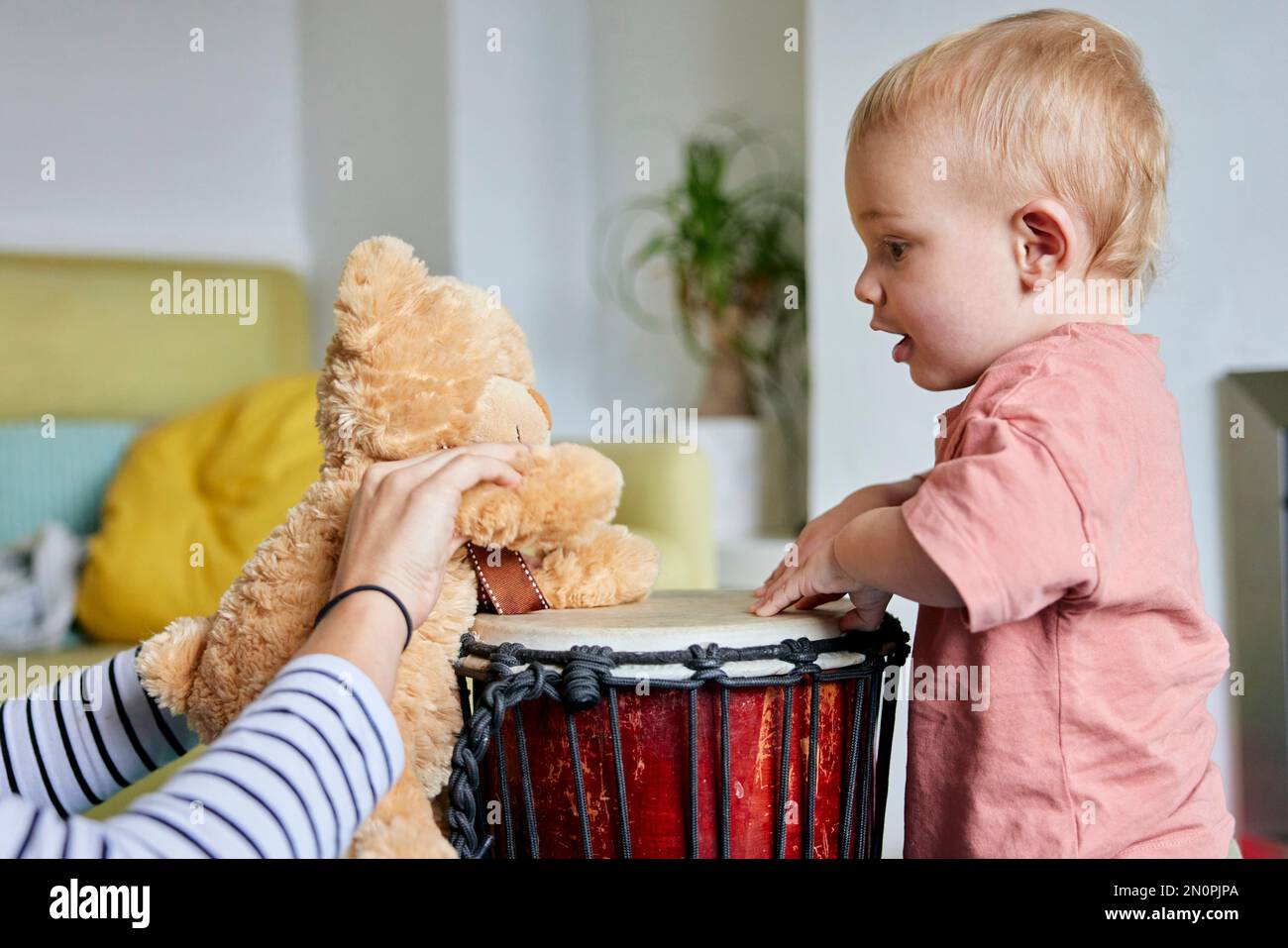 Toddler and teddy bear playing bongo drum together at home Stock Photo ...