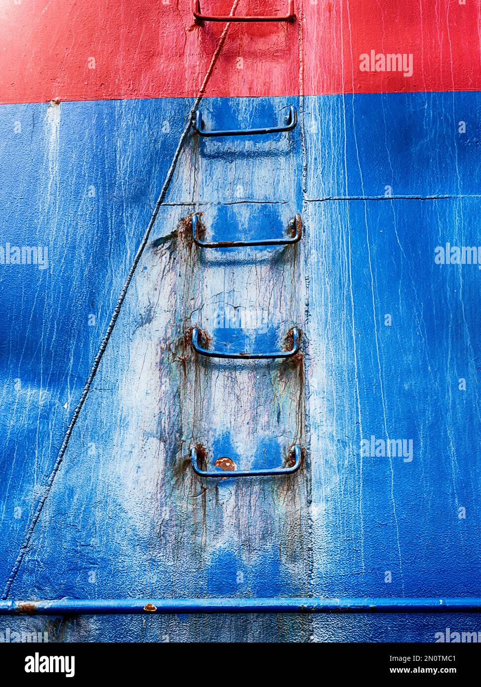 A ladder on the hull of a ship crosses sections of red and blue paint ...