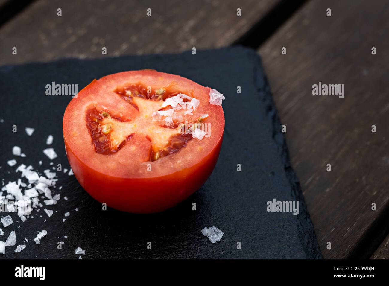 Small ripe tomato split in half with salt flakes on a black slate Stock ...