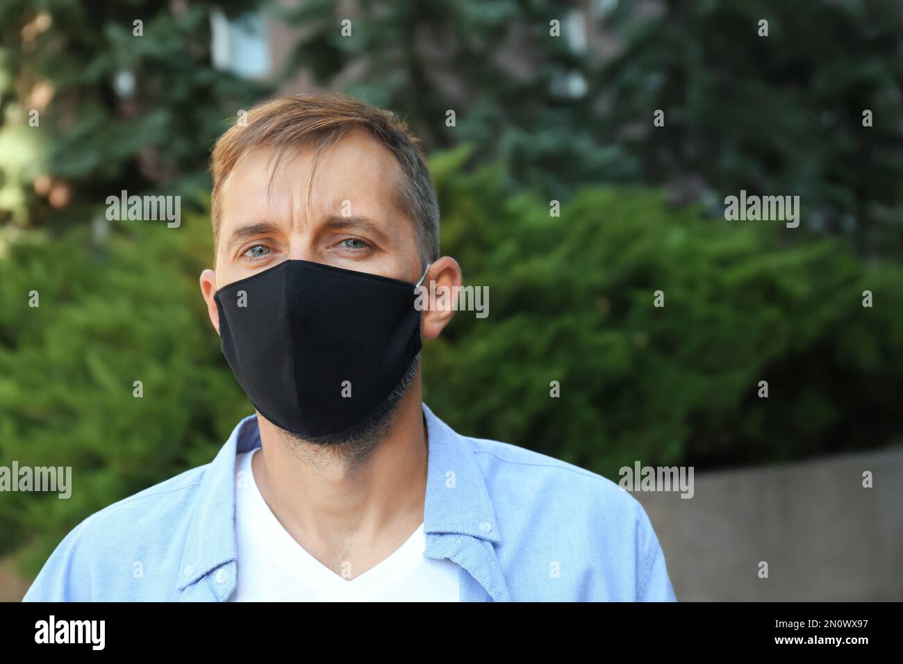 Man wearing handmade cloth mask outdoors, space for text. Personal ...