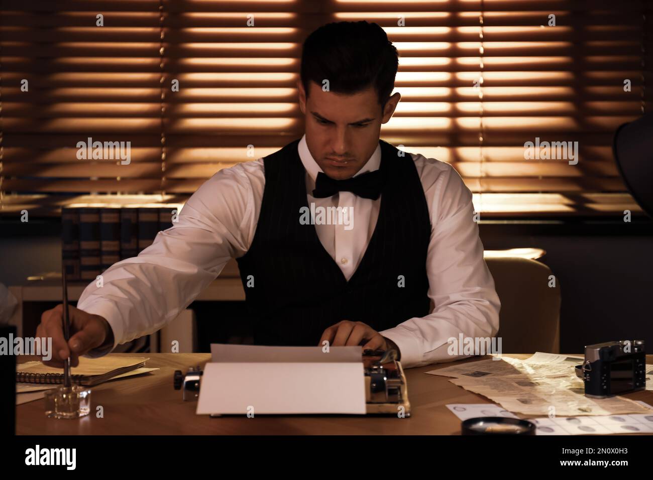 Old fashioned detective working with typewriter at table in office ...