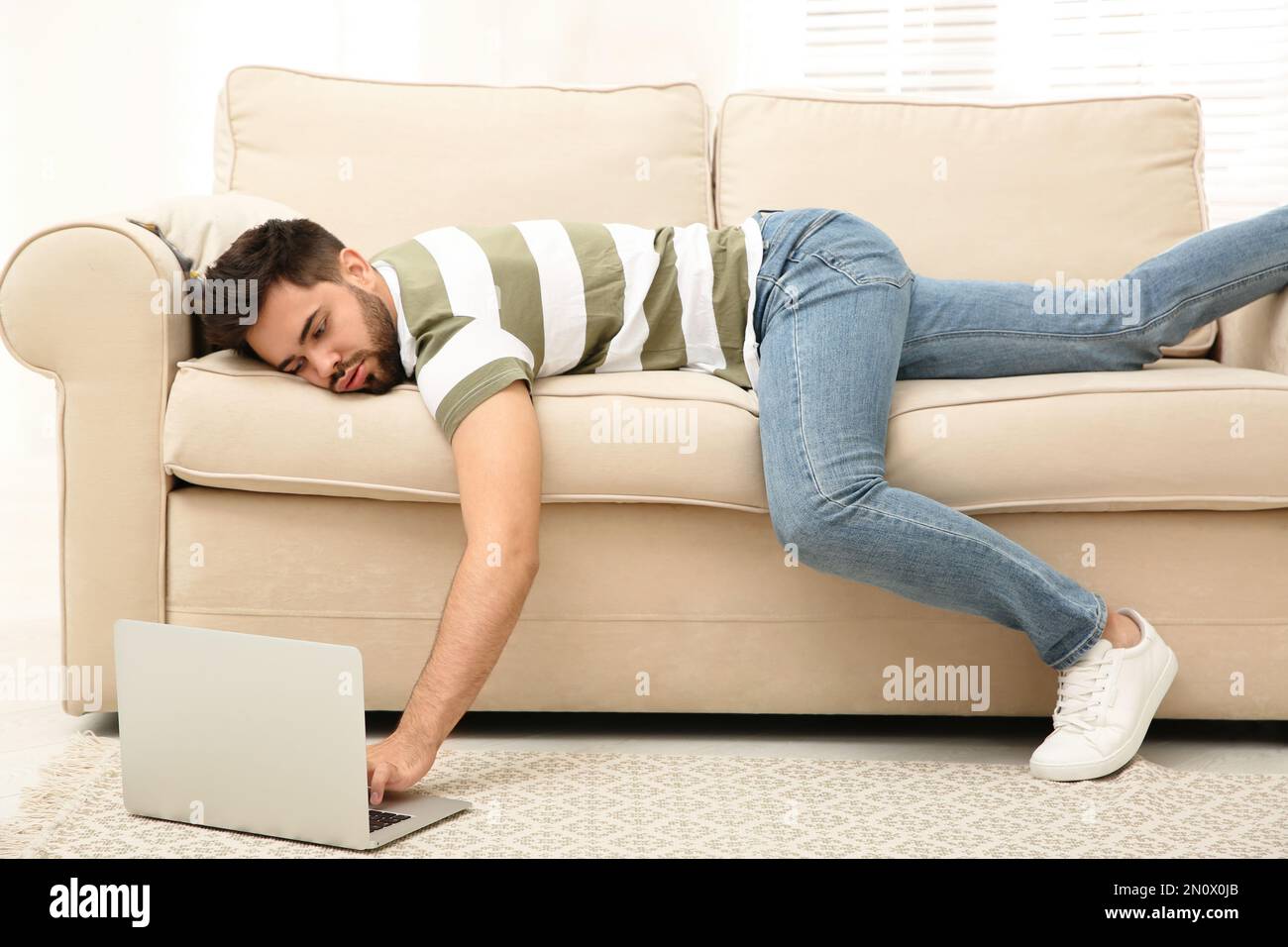 Lazy young man using laptop while lying on sofa at home Stock Photo - Alamy