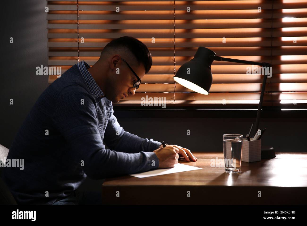 Man writing letter at wooden table in dark room Stock Photo - Alamy